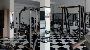 Uma academia com diversos equipamentos de exercício, piso xadrez e um espelho grande na parede.