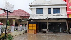 Um hotel com fachada branca, telhado de telhas vermelhas e entrada visível.