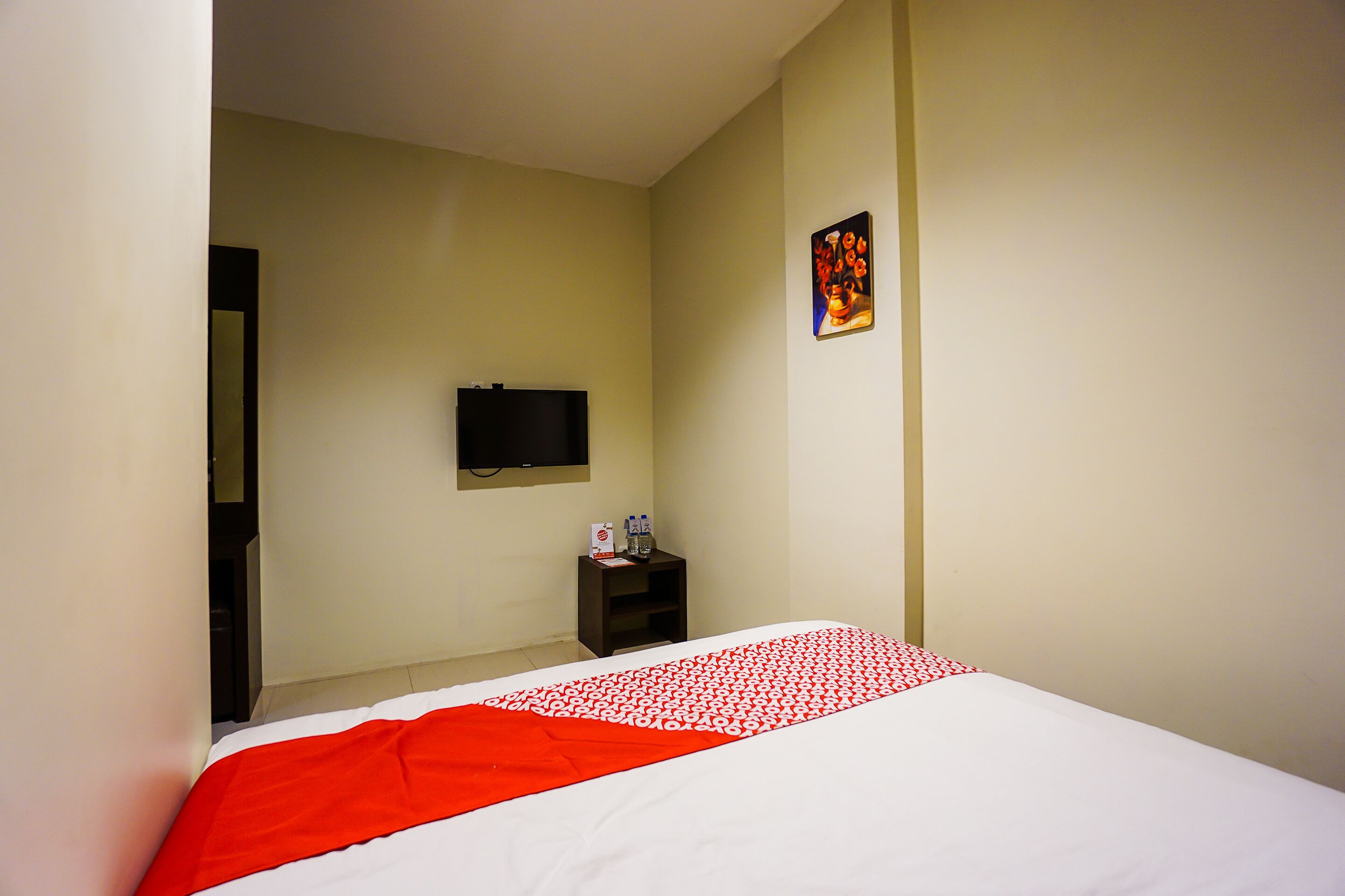 Quarto de hotel com uma cama, televisão na parede e uma mesinha com uma garrafa e uma chávena.