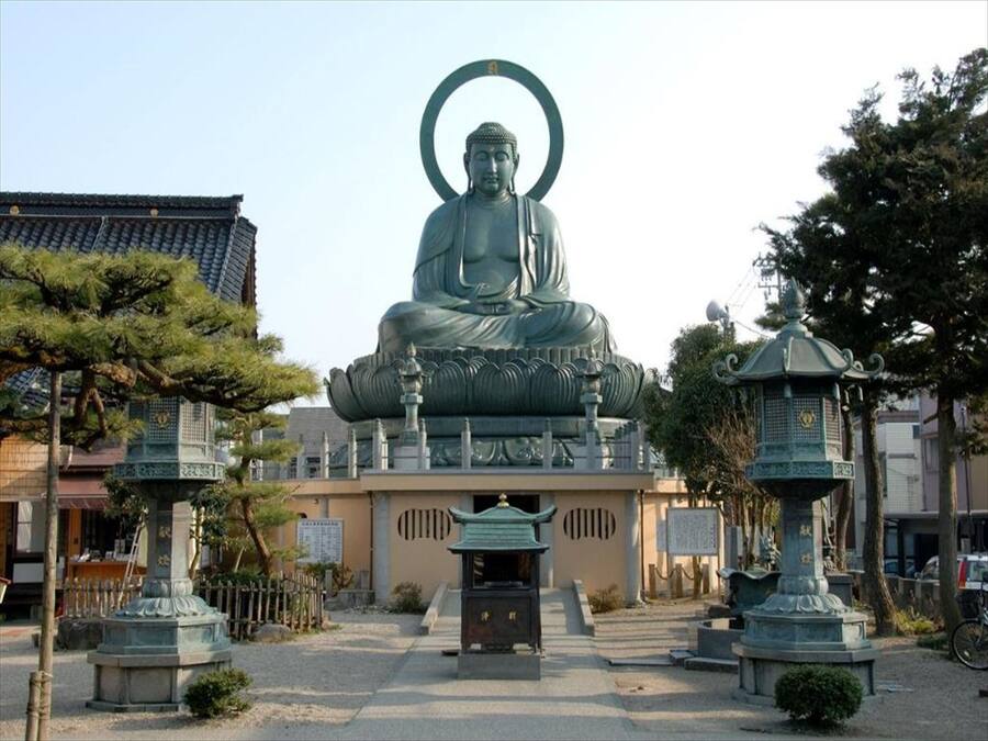 Uma grande estátua de Buda em um pátio cercado por arquitetura japonesa tradicional.