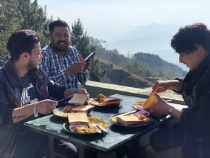 Um grupo de pessoas jantando ao ar livre com uma vista panorâmica das montanhas ao fundo.