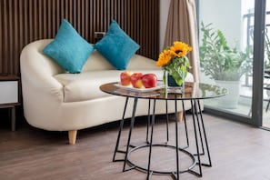 Uma sala de estar moderna com um sofá, uma mesa redonda com um vaso de flores e um prato de maçãs.