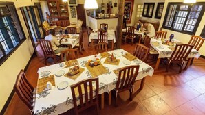 Um restaurante com várias mesas e cadeiras, decoração em madeira e chão de azulejos.