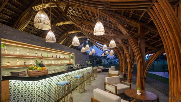 Uma área de bar com teto de bambu, banquetas e balcão com garrafas.