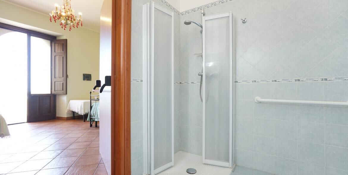 Casa de banho com chuveiro em cabine de vidro, toalheiro branco e moldura de porta de madeira.
