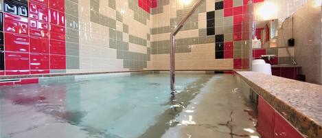 Piscina com parede revestida em padrão vermelho, cinza e branco.