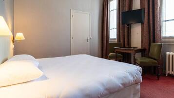 Quarto de hotel com uma cama grande, uma mesa com cadeira, televisão e janela com cortinas.