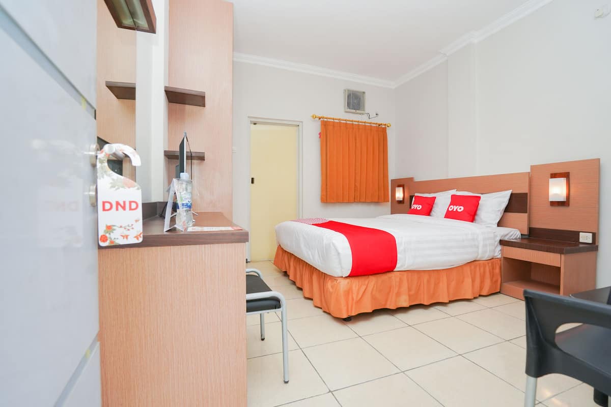 Quarto de hotel com cama, escrivaninha, cadeira e porta do banheiro.
