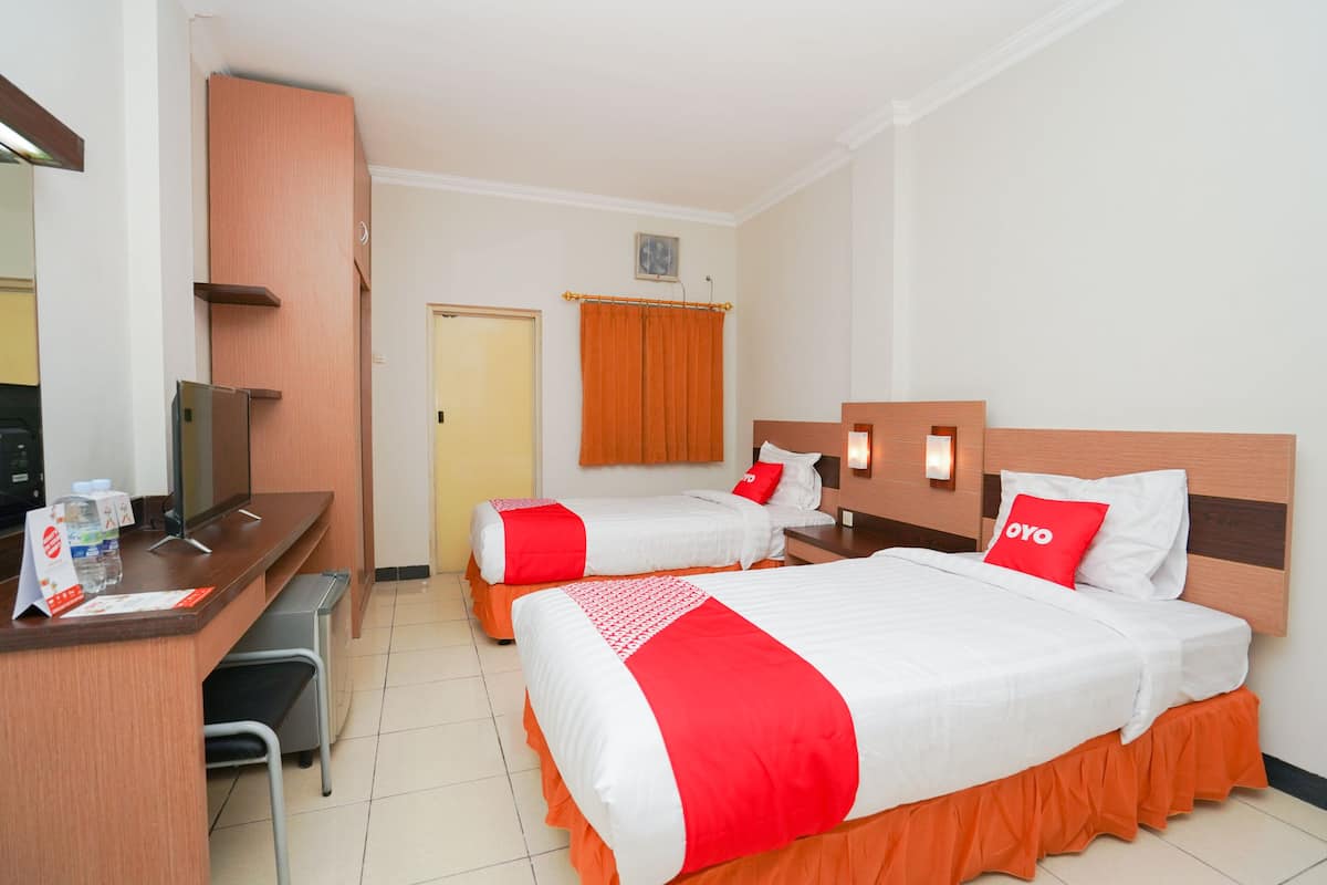 Quarto de hotel com duas camas, uma escrivaninha, uma cadeira, uma mesinha, um guarda-roupa e um banheiro.