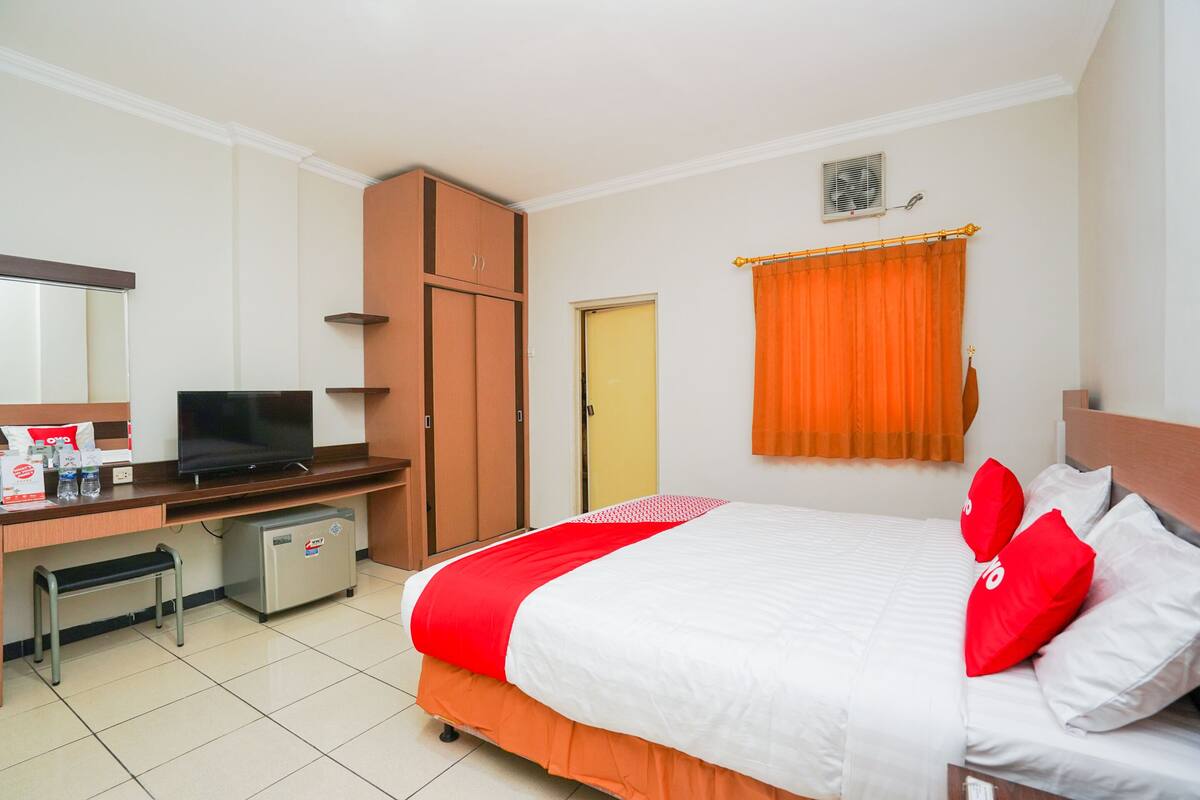 Quarto de hotel com cama, escrivaninha, televisão e armário.