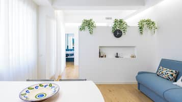 Uma sala de estar moderna com um sofá azul, uma mesa branca com uma tigela decorativa e um relógio fixado na parede.