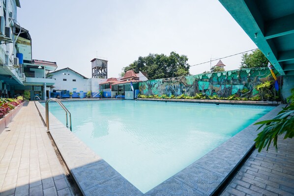 Piscina com deck revestido, cercada por edifícios e um mural.