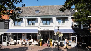Um restaurante com mesas ao ar livre, uma placa com a inscrição 'De Burg' e um telhado telhado.