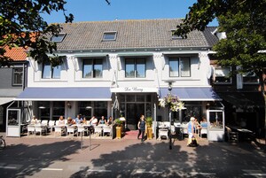 Um restaurante com mesas ao ar livre, uma placa com a inscrição 'De Burg' e um telhado telhado.