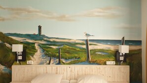 Quarto com um mural de uma praia, uma cabeceira de madeira e dois alto-falantes fixados na parede.