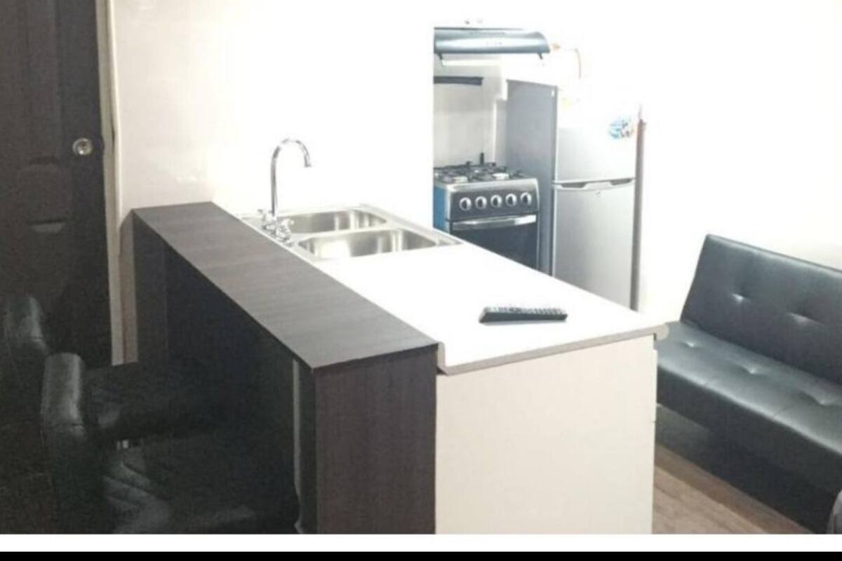 Uma cozinha compacta com bancada branca, forno embutido e sofá preto.