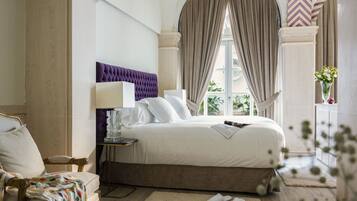 Quarto com uma cama grande, mesa de cabeceira, cadeira e janela com cortinas.