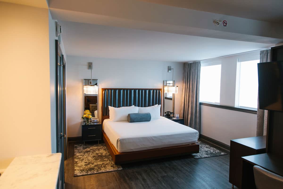 Quarto de hotel com uma cama grande, abajures, escrivaninha e televisão.
