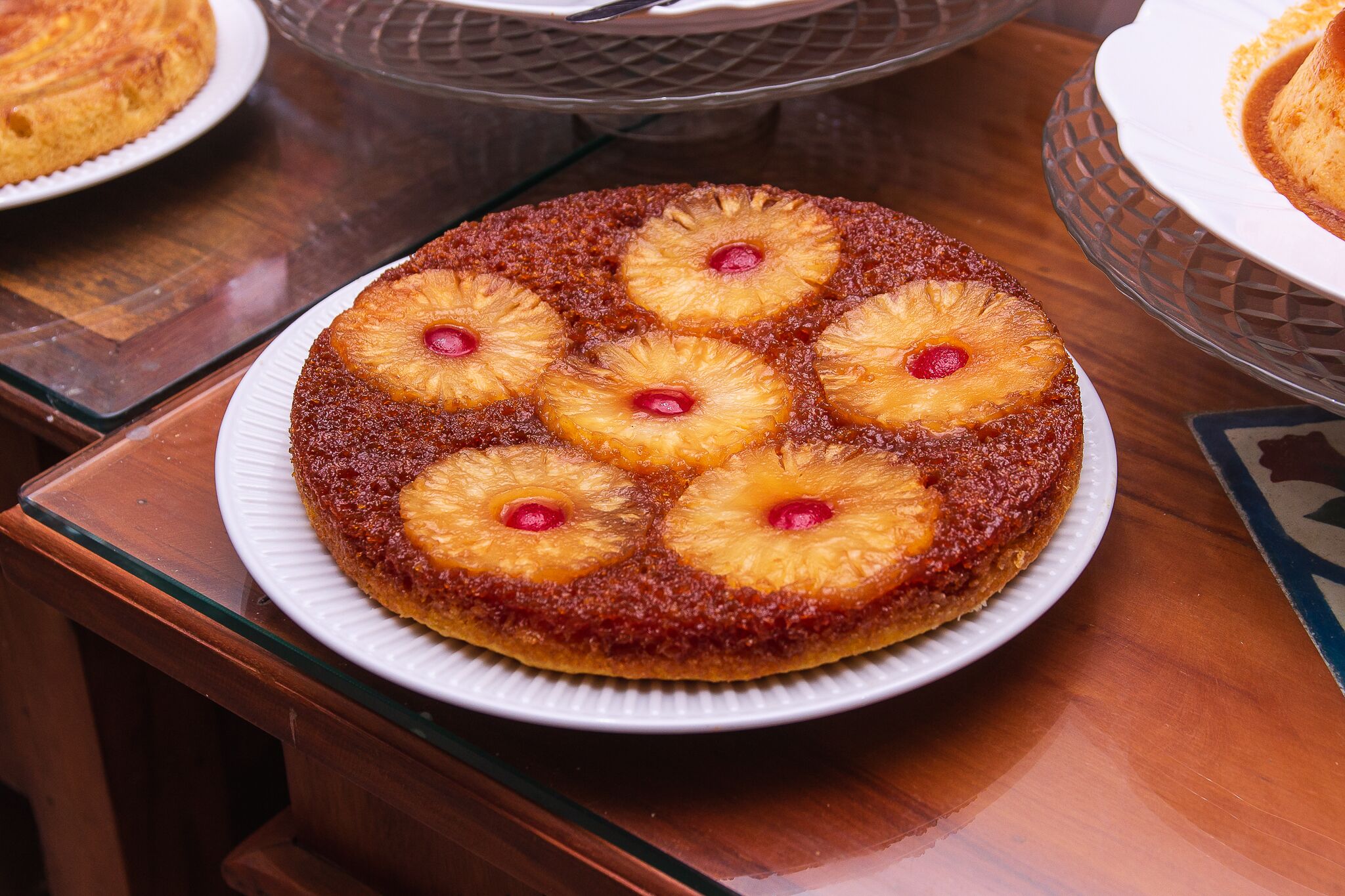 Um bolo redondo com fatias de abacaxi e cerejas numa placa branca.