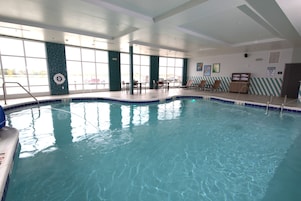 Uma piscina interior com água cristalina, uma escada de piscina e espreguiçadeiras.