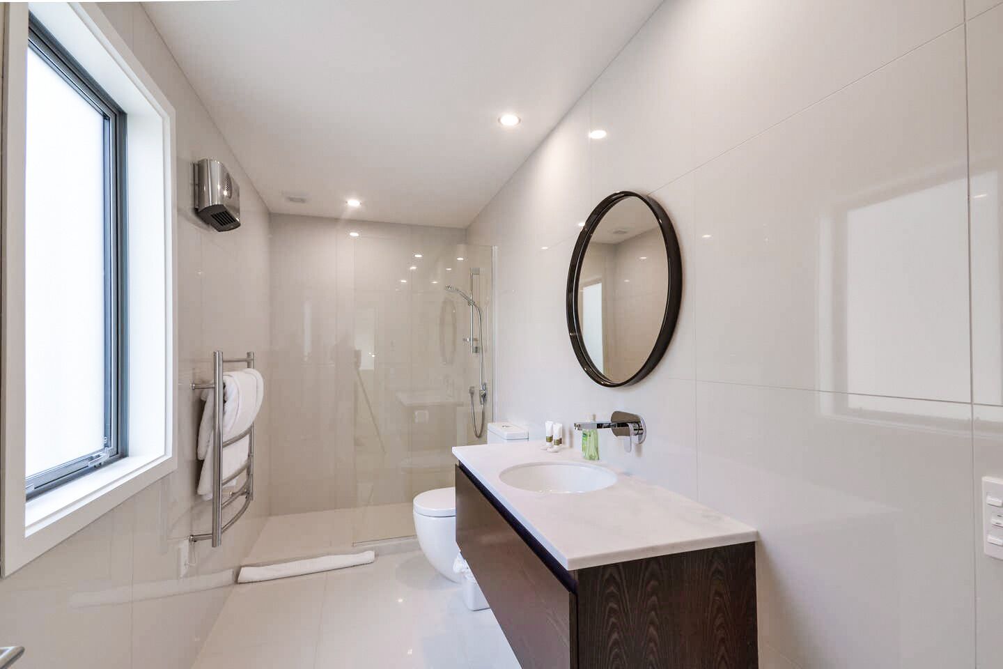 Uma casa de banho moderna com um espelho grande, sanita, chuveiro e toucador com lavatório.