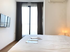 Quarto de hotel com uma cama, televisão de tela plana na parede, janela com cortinas e abajur.
