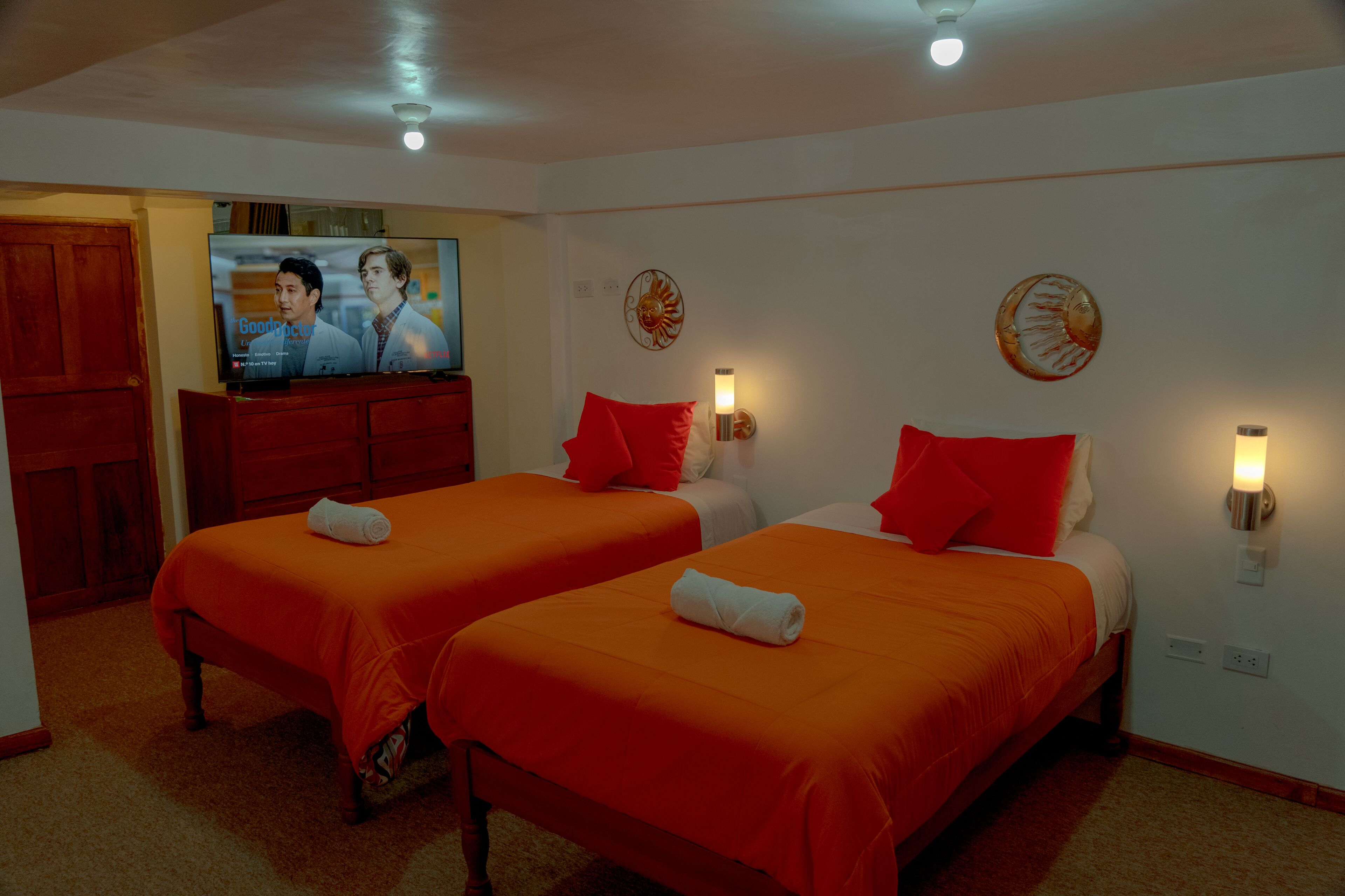 Quarto de hotel com duas camas, uma televisão e arandelas.