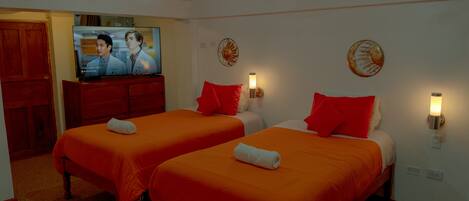Quarto de hotel com duas camas, uma televisão e arandelas.
