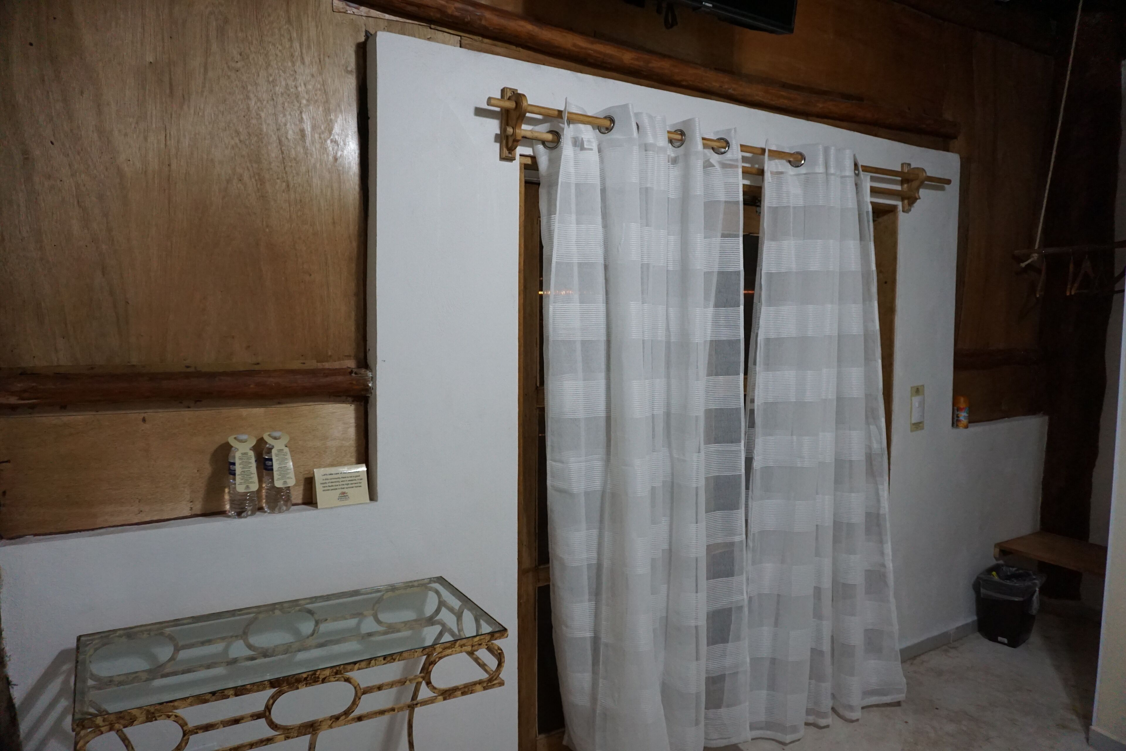 Casa de banho com porta de madeira, mesa de vidro com garrafas e cortina de chuveiro.