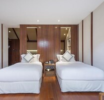 Quarto de hotel com duas camas, painéis de madeira, mesa de cabeceira com relógio e um espelho.