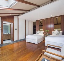 Quarto de hotel moderno com duas camas, piso de madeira e vista para a cozinha.