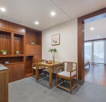 Quarto moderno com escrivaninha de madeira, duas cadeiras, uma mesinha de centro com um vaso de flores e um quadro pendurado na parede.