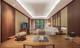 Quarto de hotel com cama, mesa de cabeceira, televisão e vista para o verde lá fora.