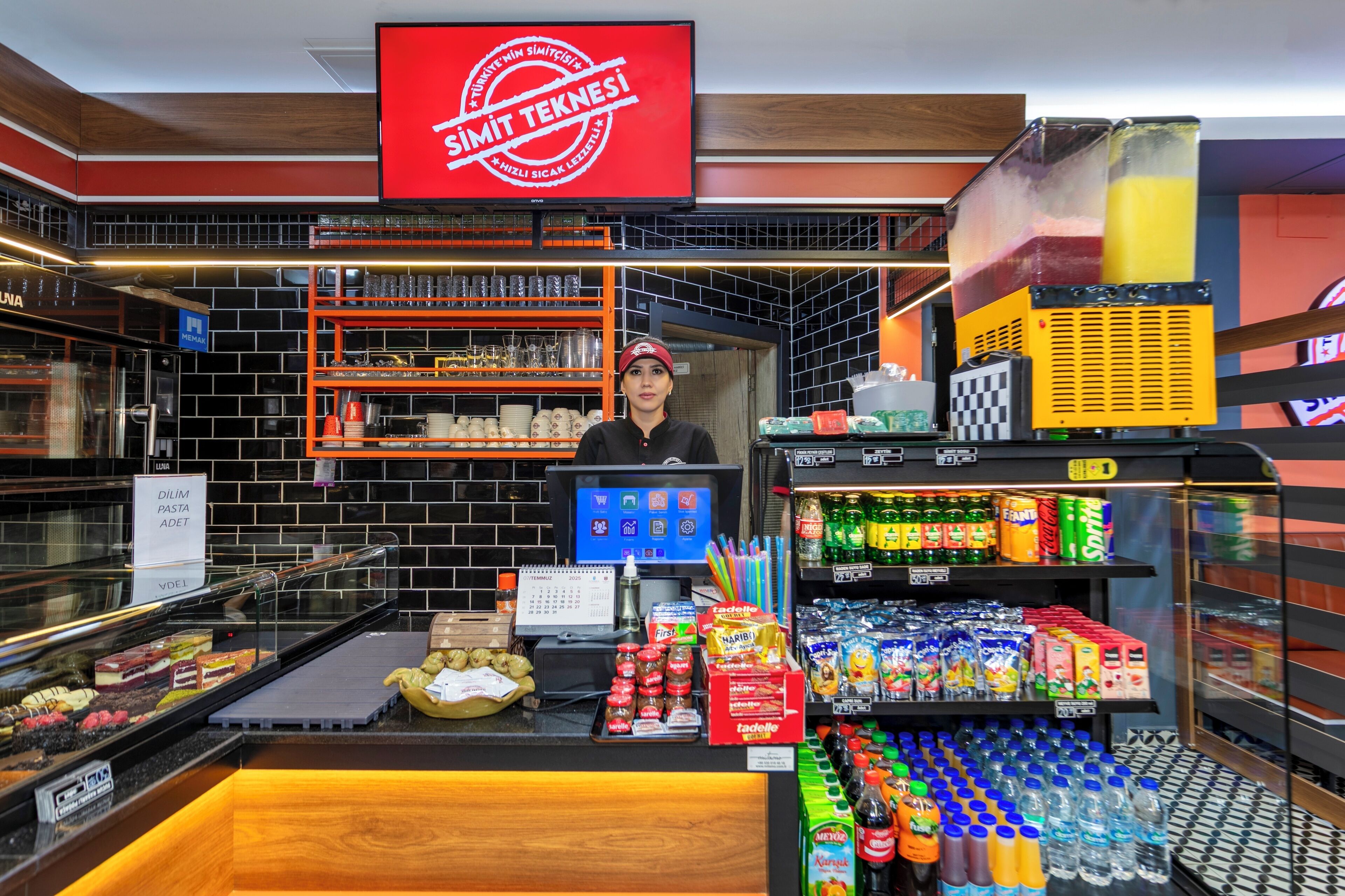 Interior moderno de um supermercado, com um visor digital, prateleiras cheias de lanches e diversas bebidas.