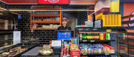 Interior moderno de um supermercado, com um visor digital, prateleiras cheias de lanches e diversas bebidas.