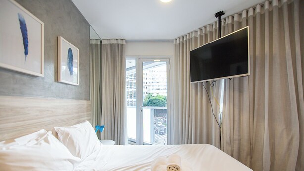Quarto de hotel com uma cama, uma televisão na parede e vista para o exterior através de uma janela.