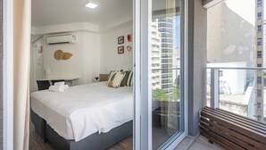 Quarto de hotel moderno com uma cama grande, um ventilador de teto e vista da cidade através de uma janela ampla.