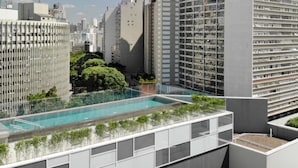 Um edifício moderno com piscina no terraço, rodeado por vegetação.