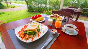 Mesa posta para o café da manhã com sanduíche, frutas e uma xícara de café.