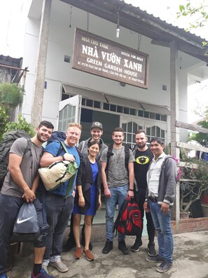 Um grupo de pessoas em frente a um edifício com uma placa que diz 'HOUSE FOR RENT GREEN GARDEN HOUSE'.