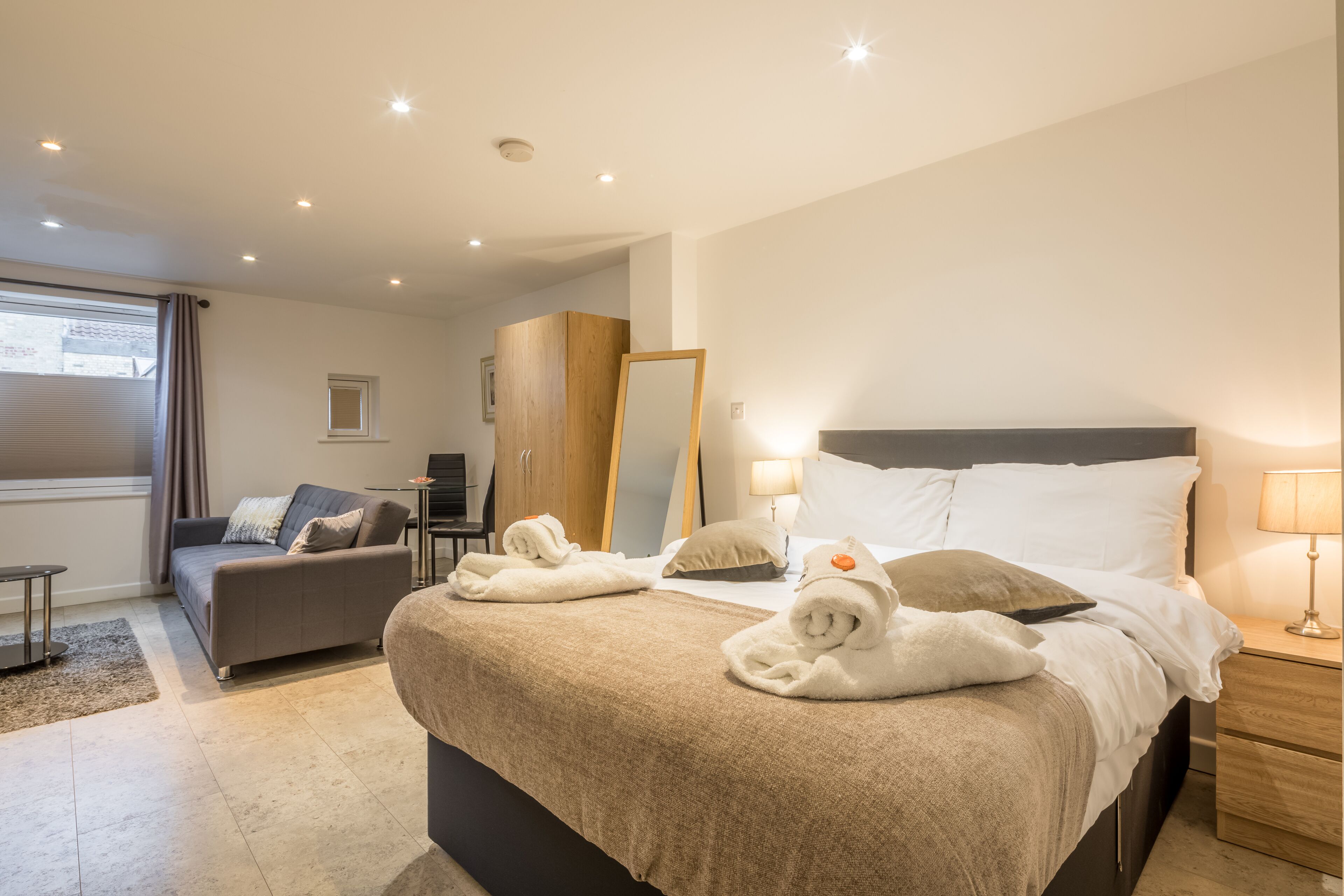 Quarto de hotel moderno com uma cama grande, um sofá, uma escrivaninha e um espelho.