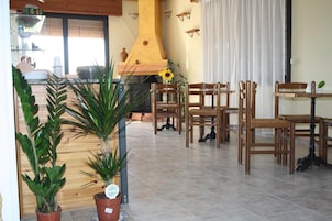 Uma sala de jantar com cadeiras e mesas de madeira, lareira de tijolos e plantas em vasos.