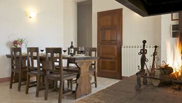 Uma sala de jantar com mesa e cadeiras de madeira, um vaso com flores e uma garrafa de vinho.