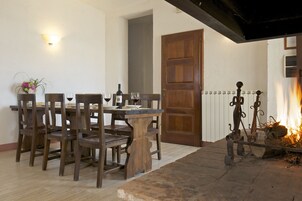 Uma sala de jantar com mesa e cadeiras de madeira, um vaso com flores e uma garrafa de vinho.