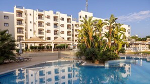 Um hotel com piscina, área de estar ao ar livre e um edifício grande com várias varandas.