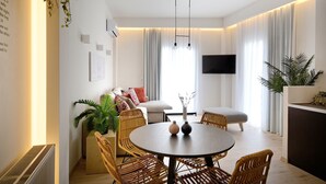 Uma sala de estar moderna com uma mesa de jantar redonda, cadeiras de vime, um sofá e uma televisão de tela plana.