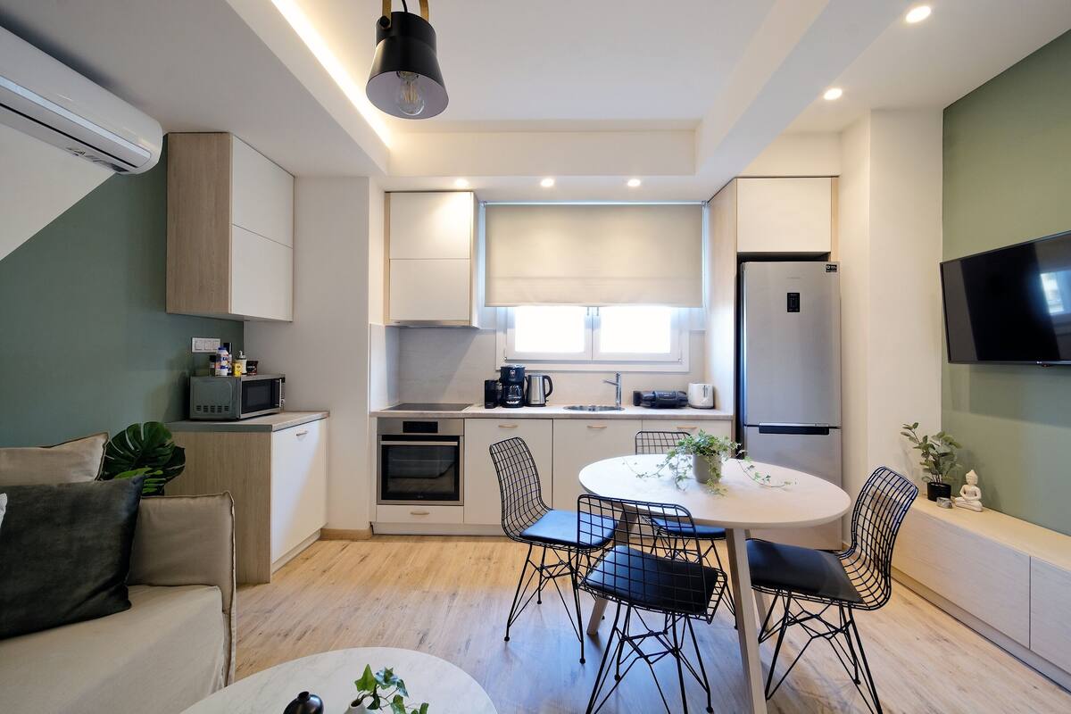 Cozinha moderna com armários brancos, micro-ondas e frigorífico. Dispõe de um espaço de refeições com uma mesa redonda e cadeiras.