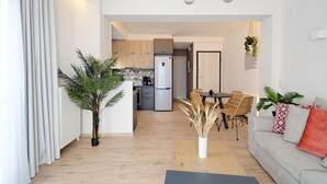 Uma sala de estar moderna com sofá, mesa de jantar com cadeiras e área de cozinha com geladeira e armários.