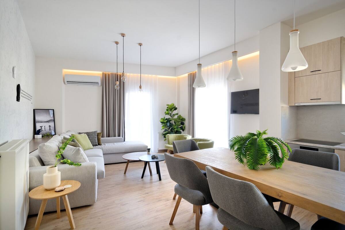 Uma sala de estar moderna com sofá, mesa de jantar, cadeiras, uma pequena mesa lateral e uma planta em vaso.