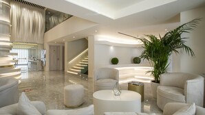 Um hall moderno com piso de mármore, escada e área de estar com mesa redonda e cadeiras.
